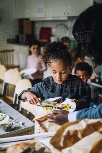 Girl throwing leftover food in paper bag held by teacher at child care ...