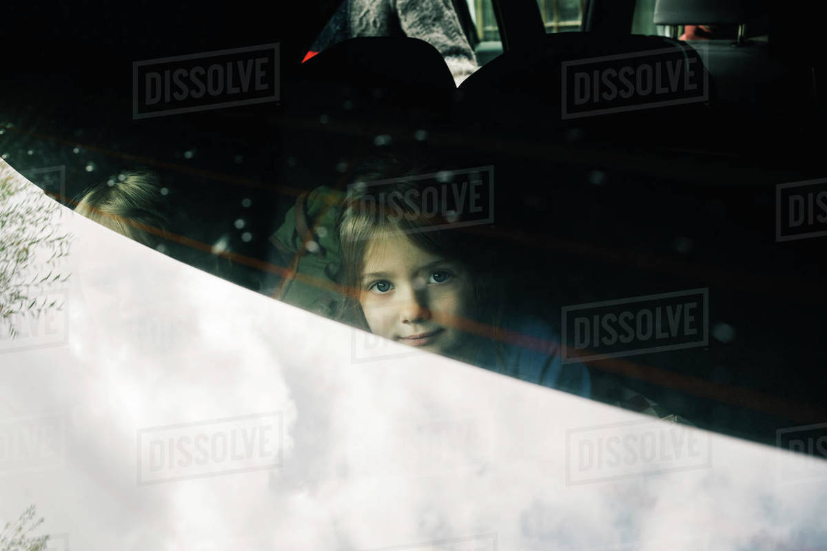 Portrait of girl sitting in electric car trunk seen through rear ...