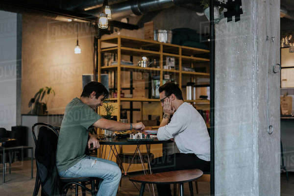 Male business colleagues playing chess on table at office cafeteria ...