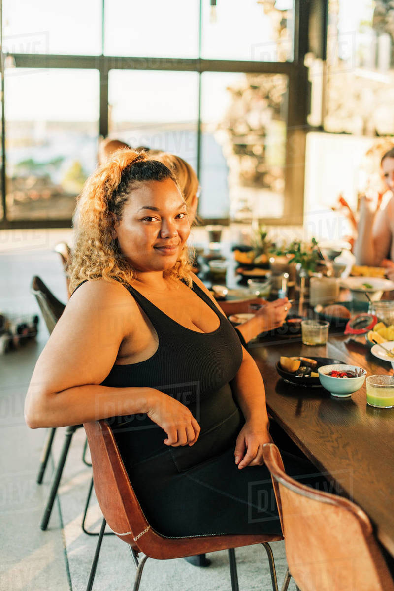 Portrait of smiling plus size woman sitting on chair with breakfast at ...