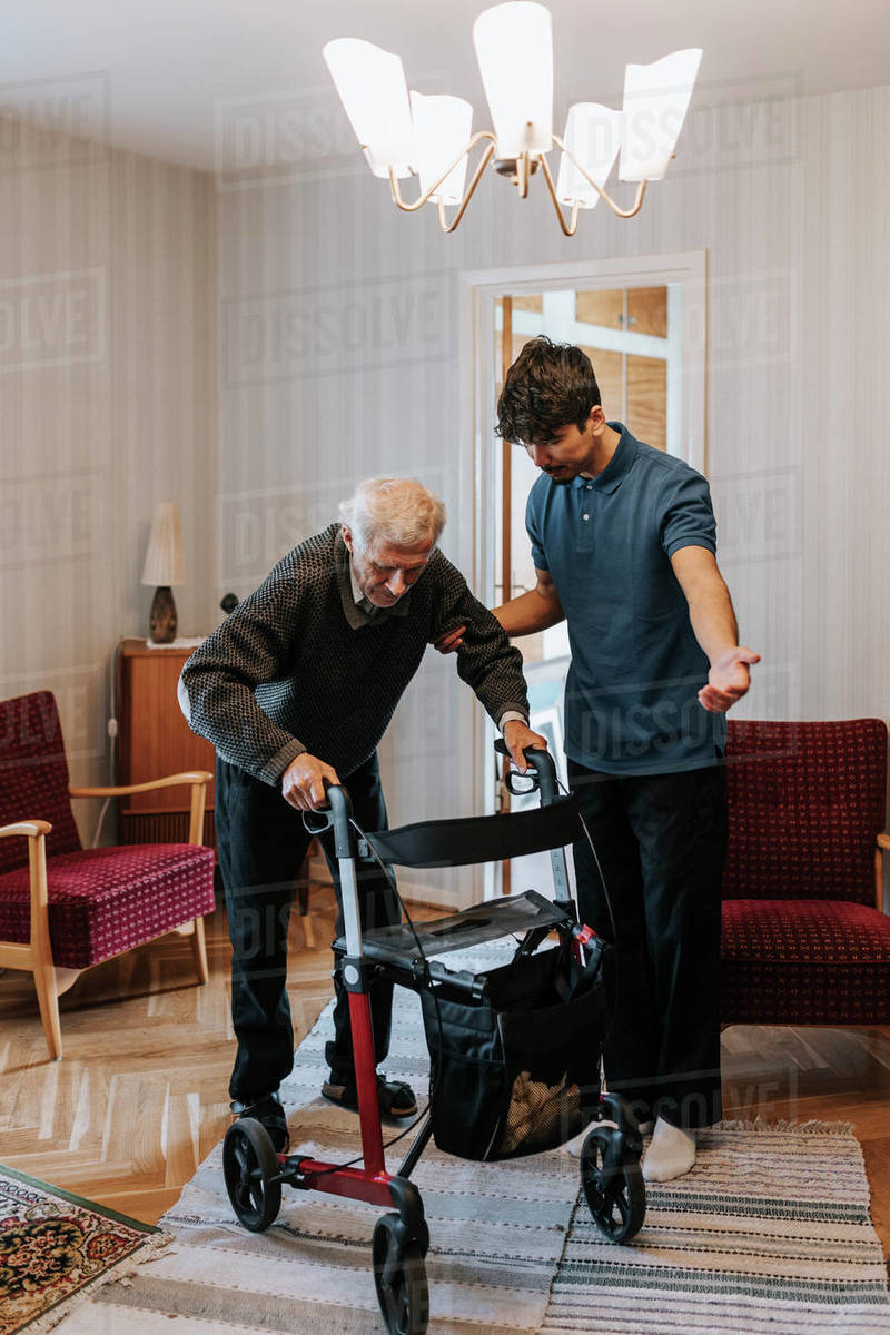 Male healthcare worker supporting senior man using mobility walker at ...