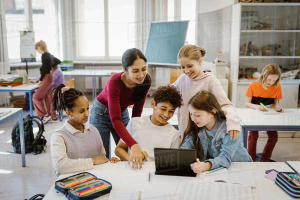 Teacher with male and female students using tablet PC at desk in ...