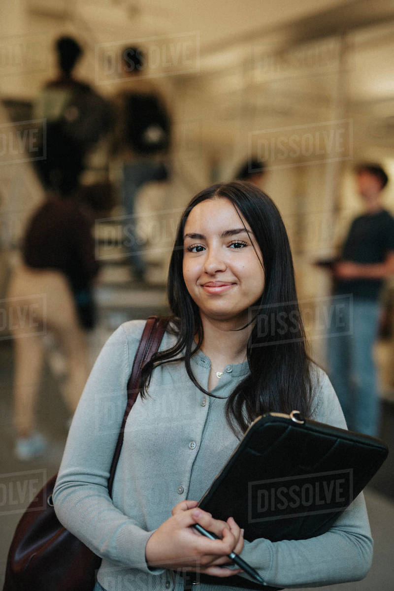 Portrait of confident female student carrying file folder standing in ...