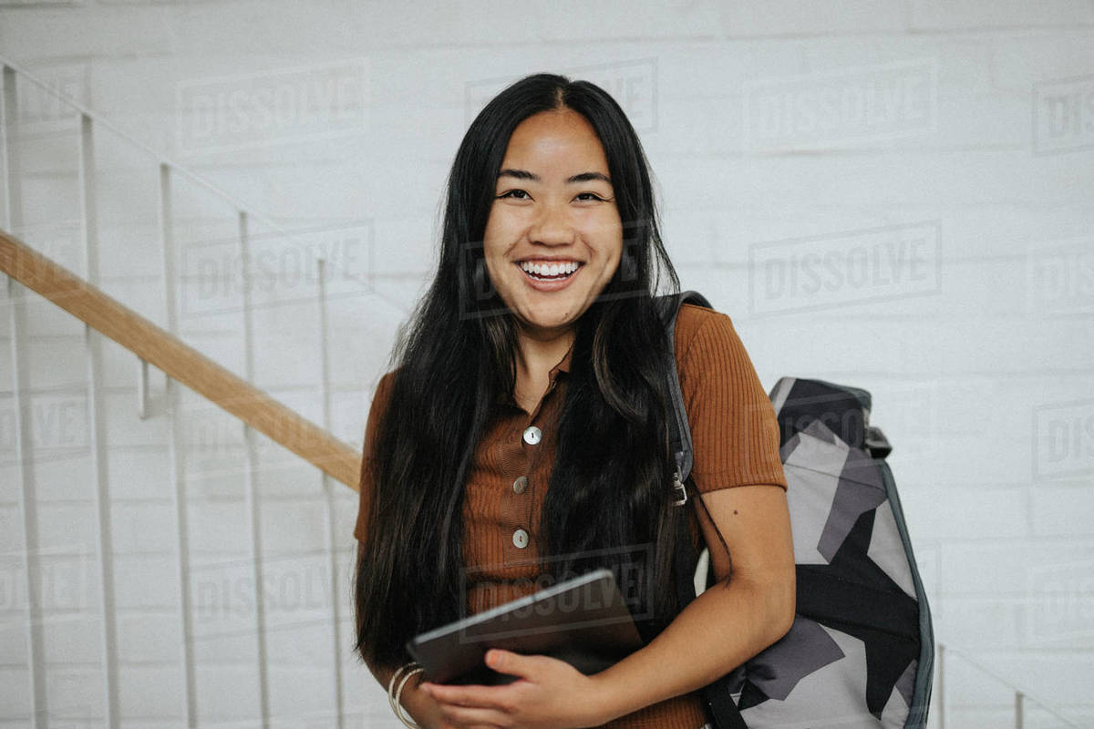 Portrait of cheerful student carrying backpack standing in university ...