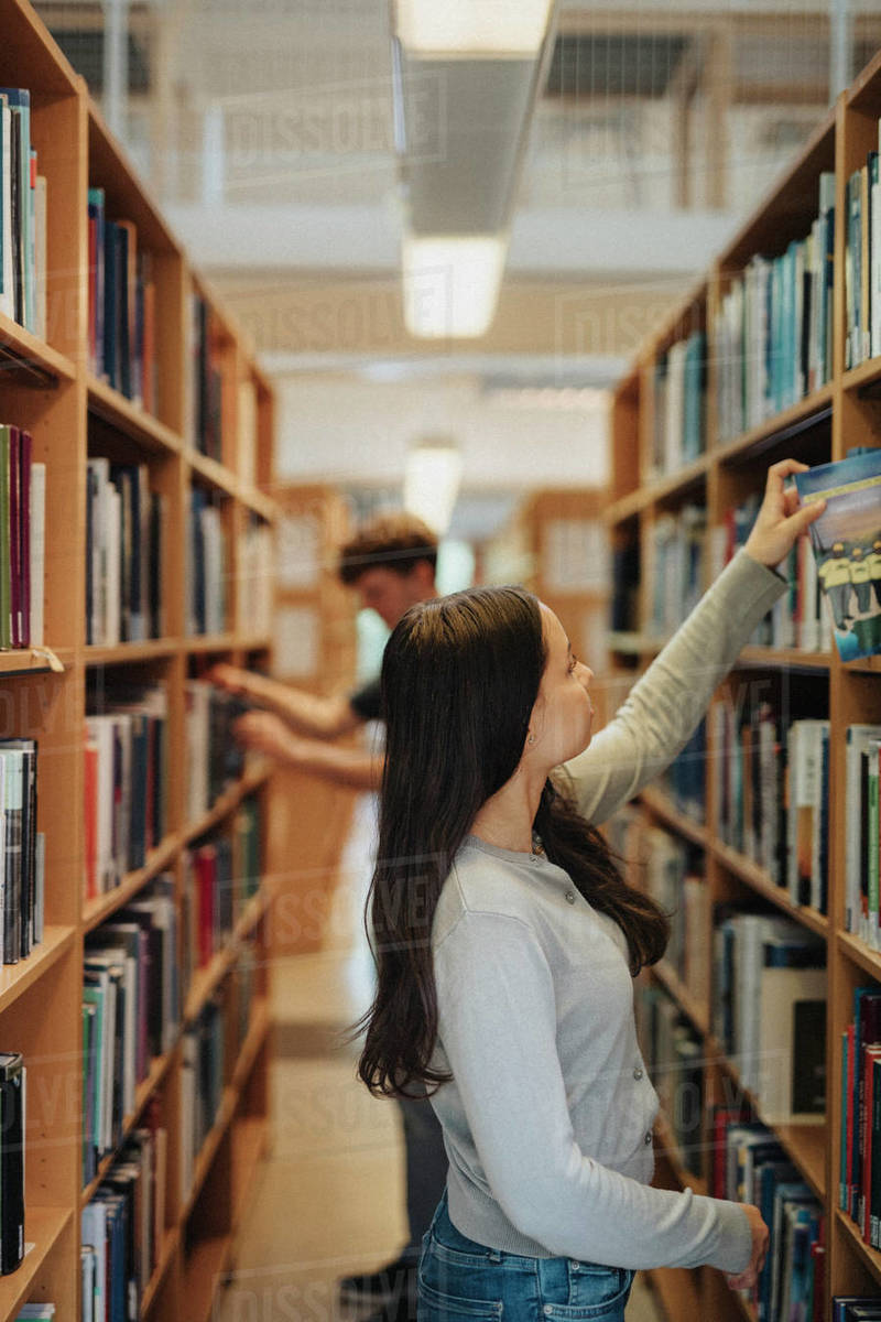 Side view of female student searching books on bookshelf in library at ...