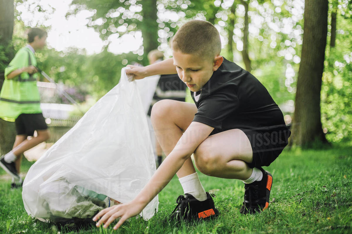 Full length of boy squatting and collecting garbage in bag - Stock ...
