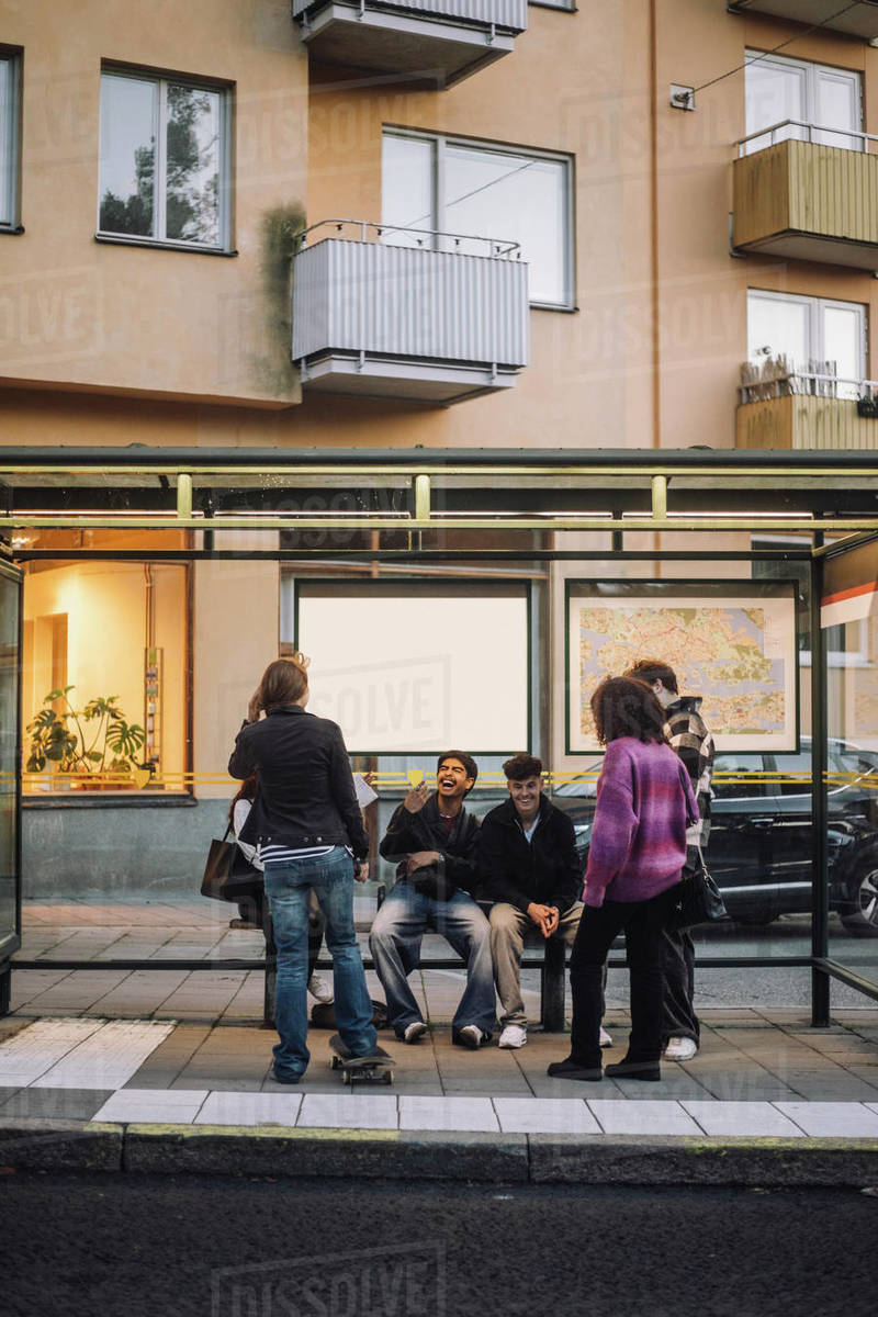 Happy male and female friends having fun at bus stop in city - Stock ...