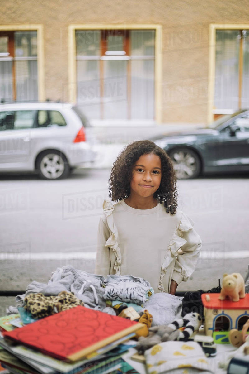 Portrait of smiling girl standing with hand on hip near stall at flea ...