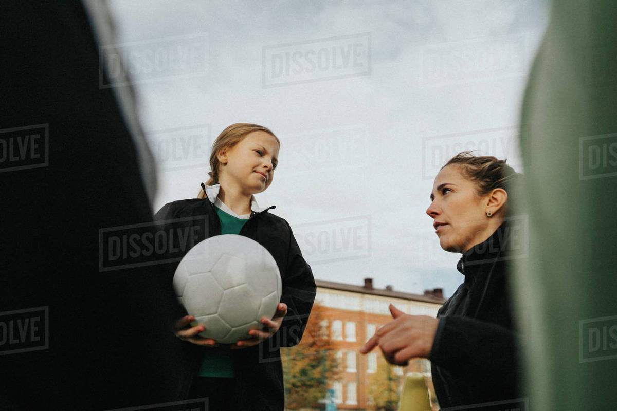 Female coach giving advice to elementary girl with sports ball against ...
