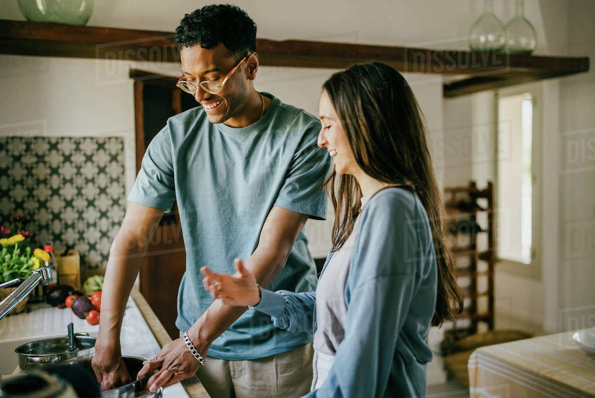 Happy young man and woman washing dishes together in kitchen sink at ...