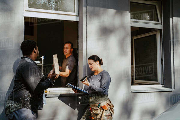 Workers passing plank through window while female construction manager ...
