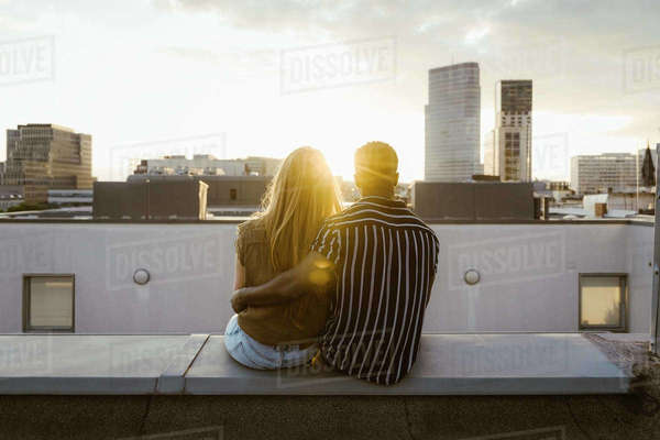 Rear view of boyfriend and girlfriend sitting on terrace and looking at ...