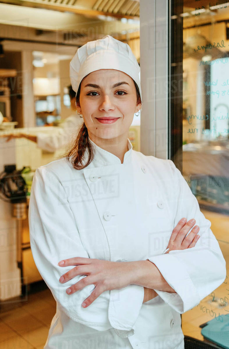Happy female chef with arms crossed standing at door in commercial ...