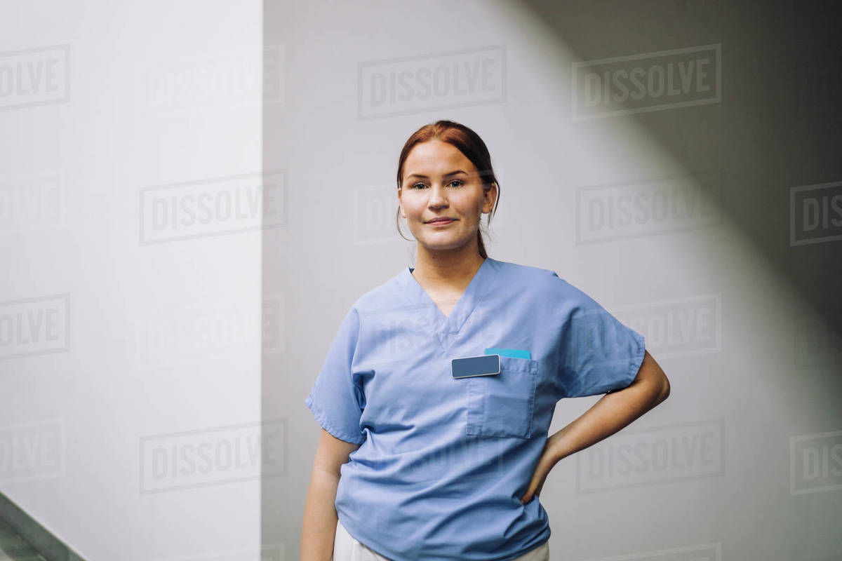 Portrait of smiling young female medical trainee standing with hand on ...