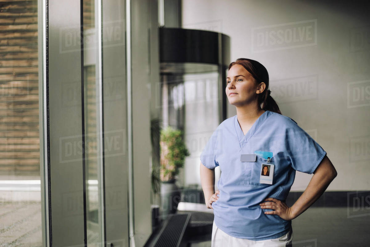 Young female medical trainee standing with arms akimbo near window in ...