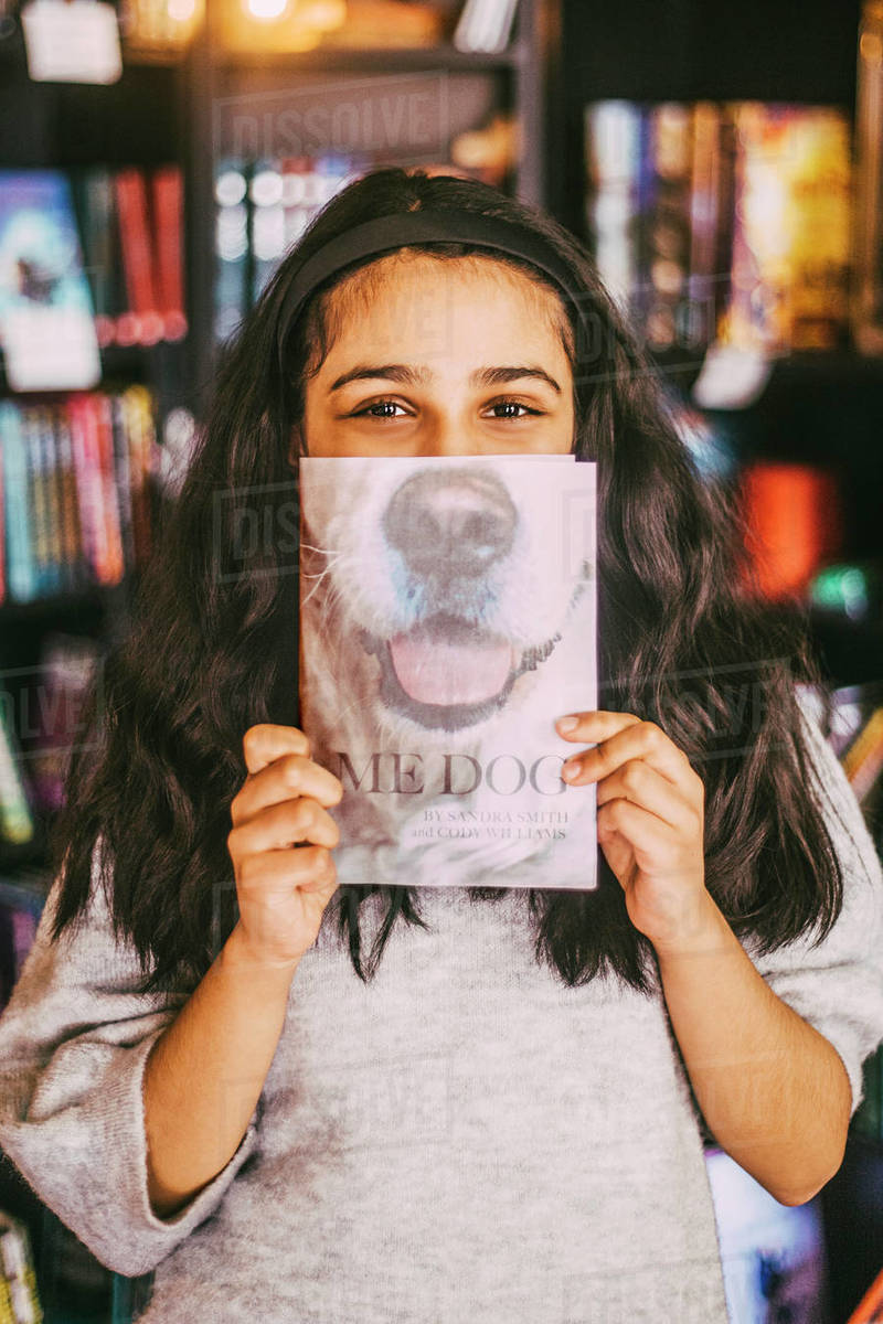 Portrait of girl showing book cover while standing in bookstore ...