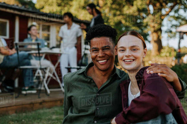 Portrait of happy young man with arm around female friend in back yard ...