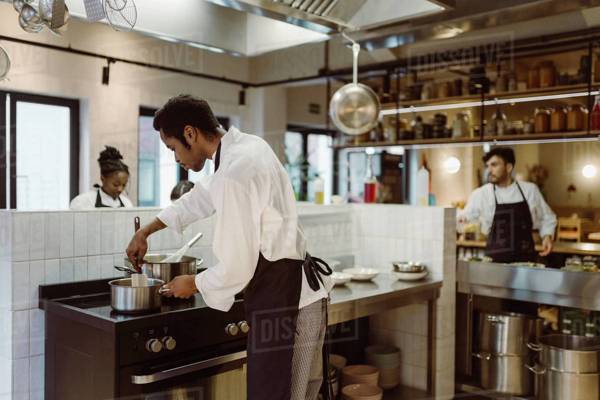 Male and female chefs cooking food at commercial kitchen in restaurant ...