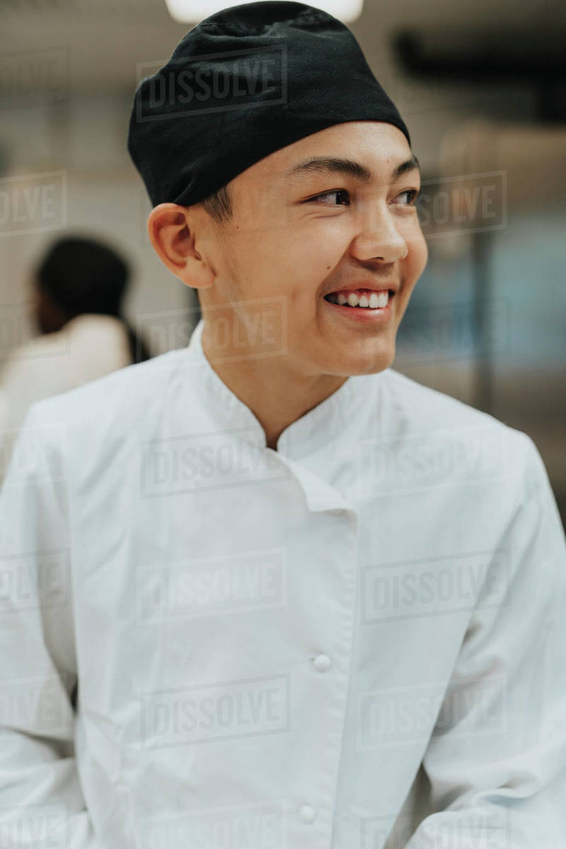 Happy male teenage trainee wearing chef's hat at culinary school ...