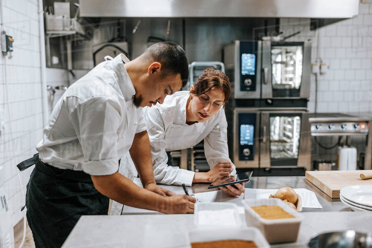 Female chef holding tablet PC while talking with male coworker taking ...