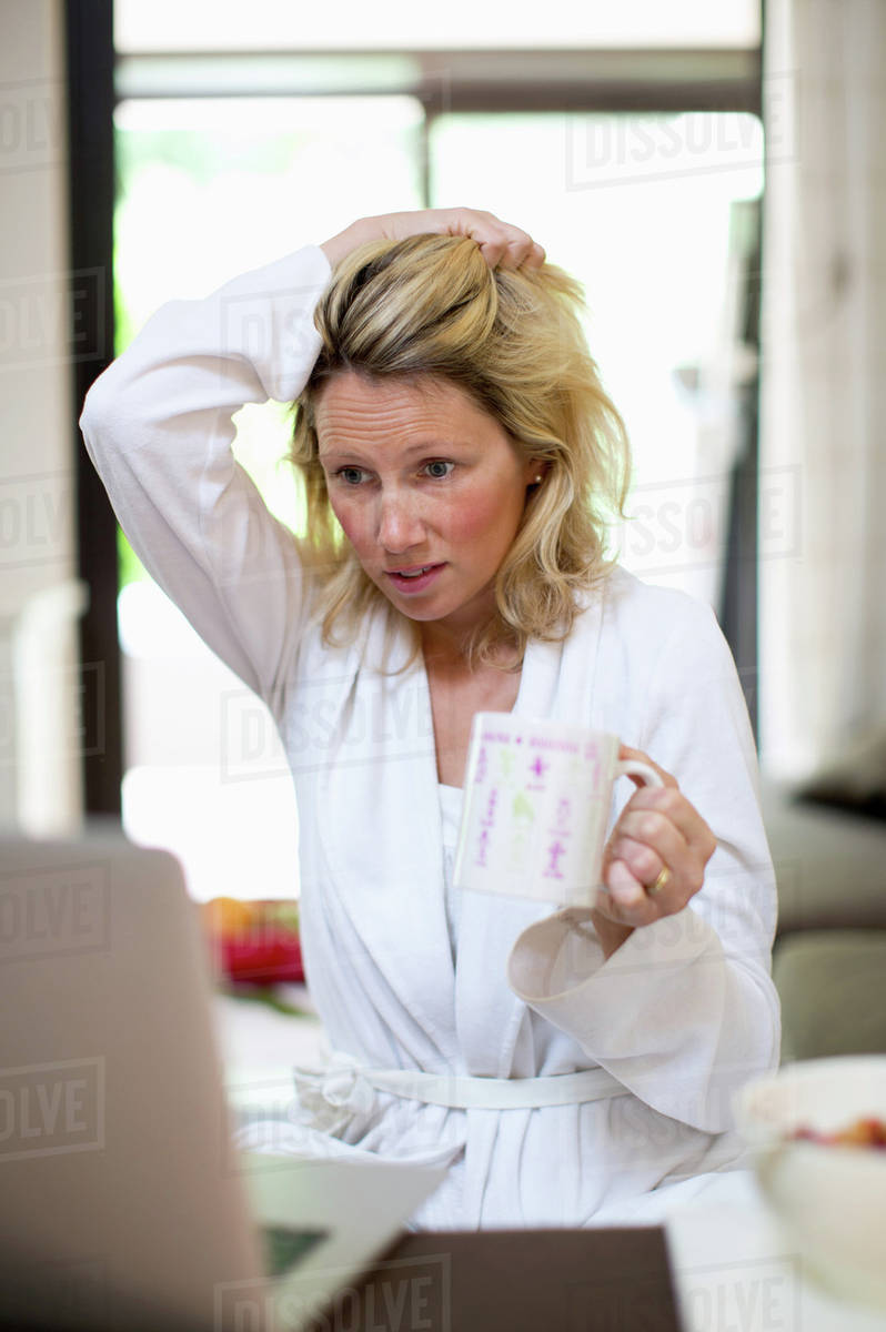 Distraught woman with coffee cup working on laptop at home - Royalty ...