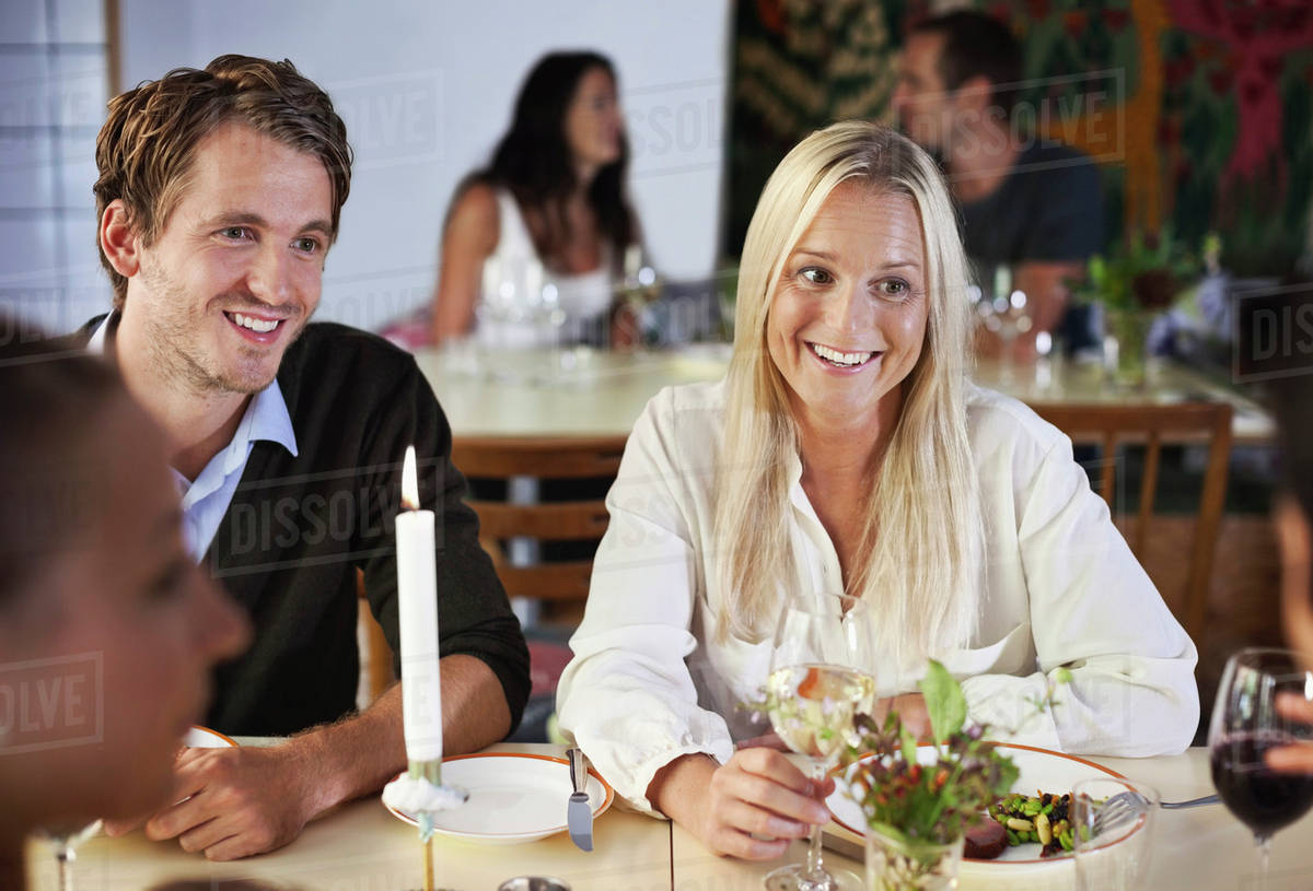 Happy friends sitting at restaurant table with people in the background ...