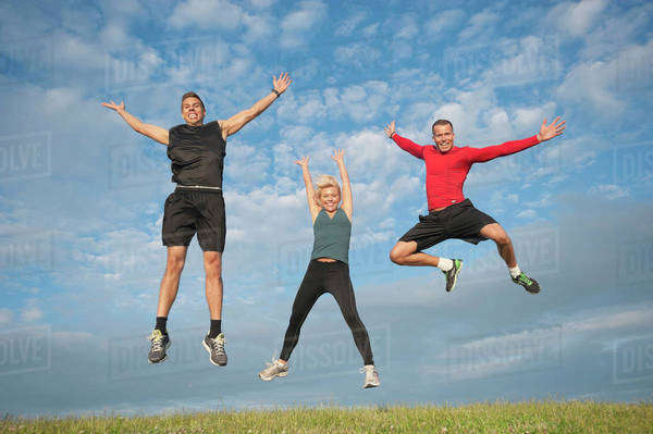 Full length of young athletes jumping in field over clouds sky - Stock ...