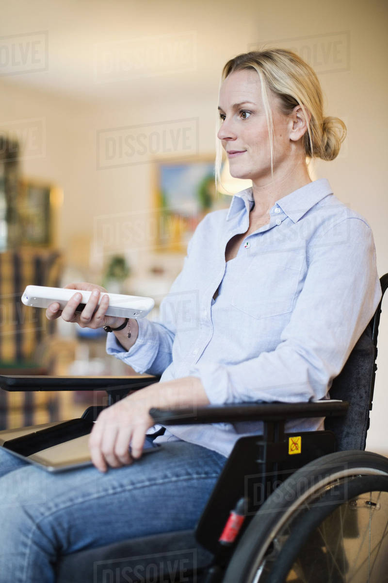 Disabled woman in wheelchair with digital tablet using remote control ...