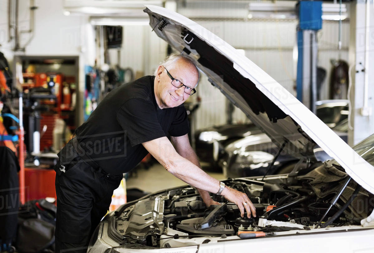 Portrait of confident male mechanic working under car bonnet in ...