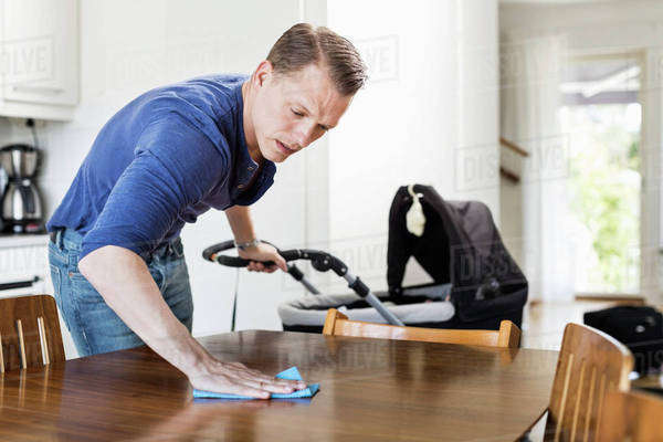 Man cleaning dining table while holding baby carriage in kitchen ...