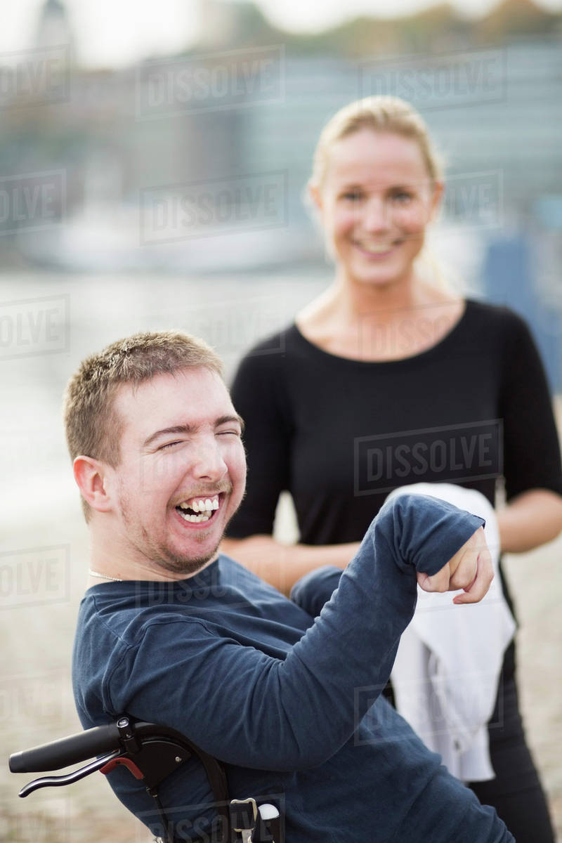 Disabled man on wheelchair laughing by caretaker outdoors - Royalty ...