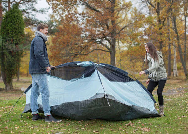 Full length of young couple pitching tent in forest - Royalty-free ...