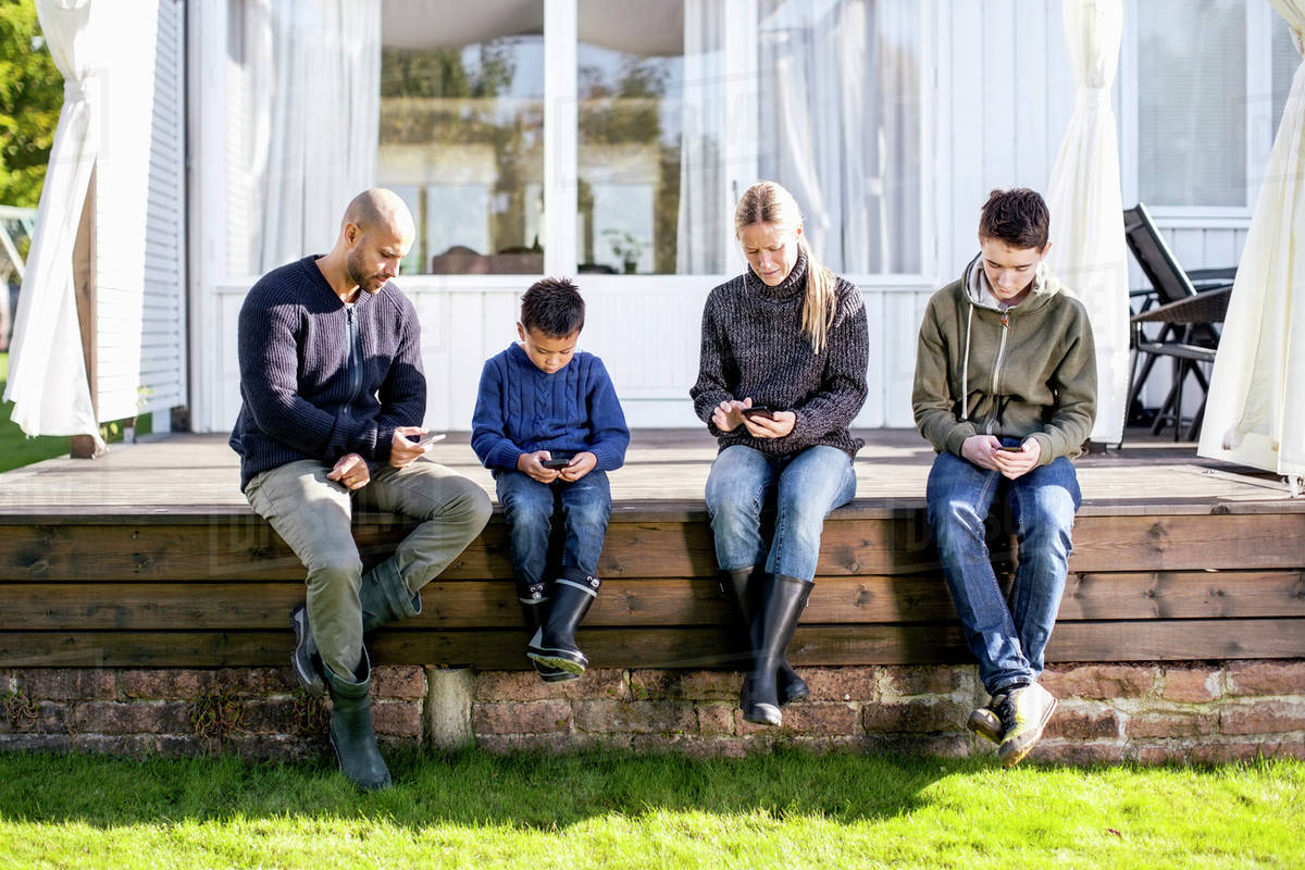 Family of four using mobile phones at yard - Royalty-free Stock Photo ...