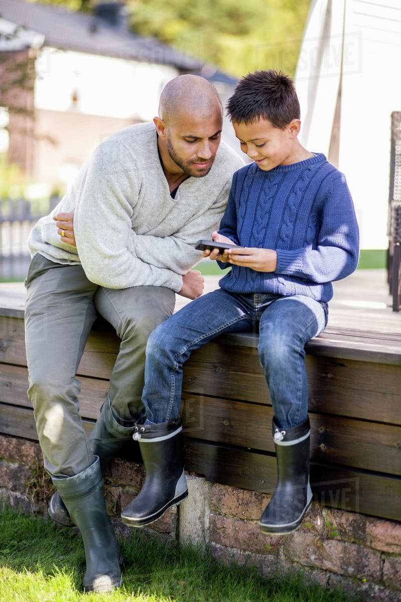 Father and son using mobile phone at yard - Stock Photo - Dissolve