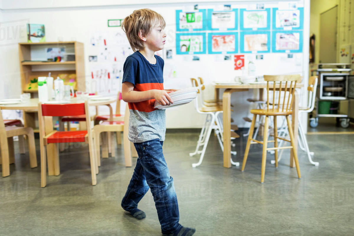 Elementary boy carrying plates in kindergarten - Stock Photo - Dissolve