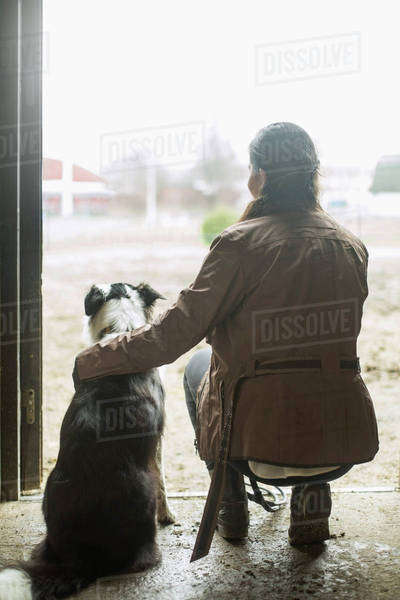 Full length rear view of young woman arm around dog in doorway of horse ...