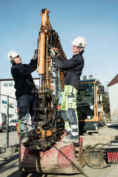 Side view of construction workers using excavator against blue sky ...