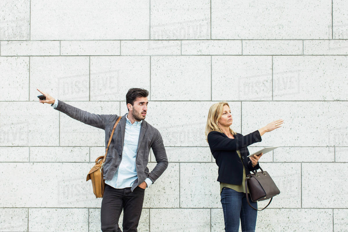 Business colleagues pointing opposite directions against wall outdoors ...