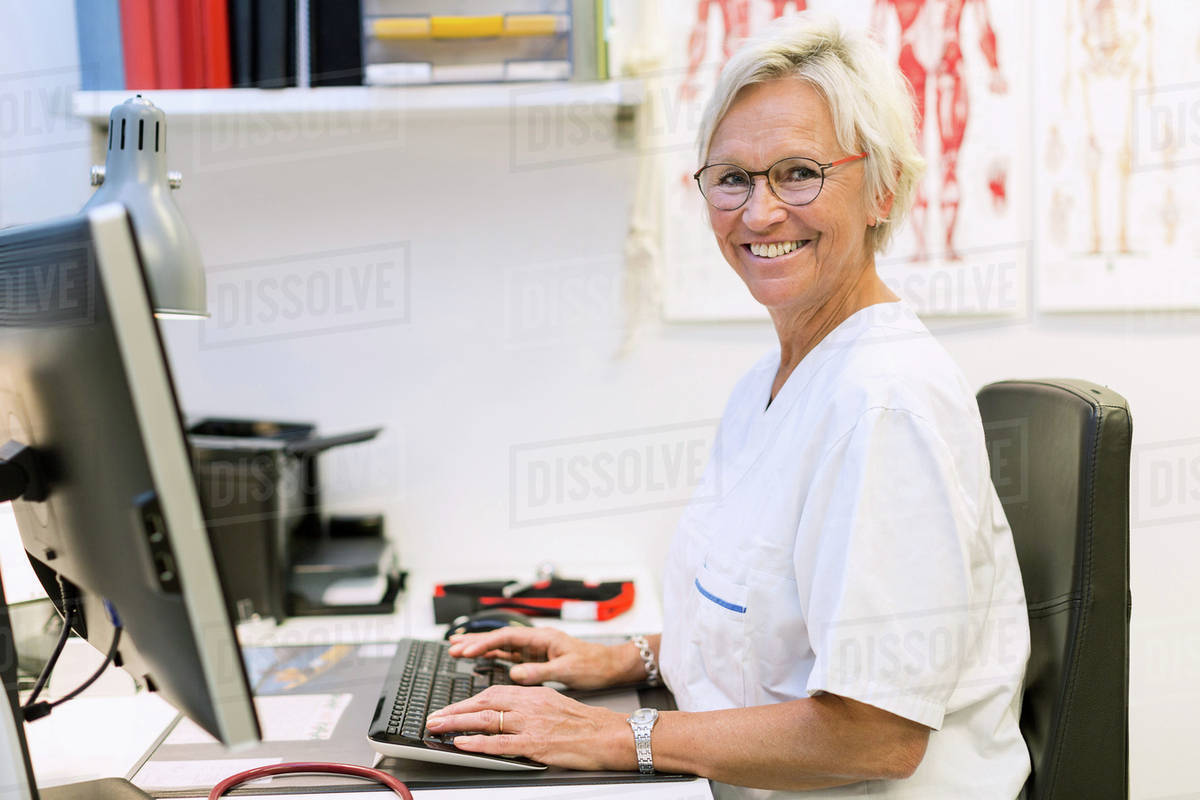 Portrait of happy senior orthopedic surgeon using computer at desk in ...