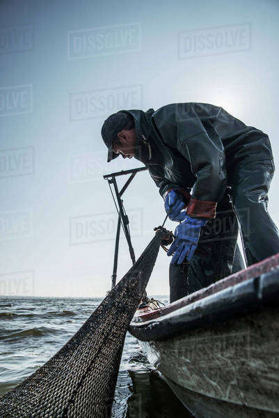 Fisherman pulling fishing net while standing on boat against clear sky ...