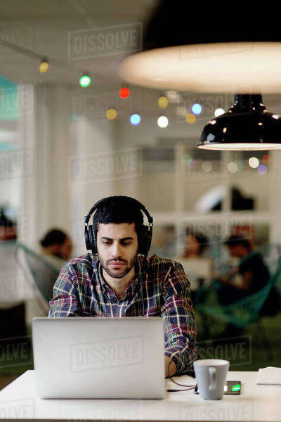 Businessman listening music while working late on laptop in creative ...
