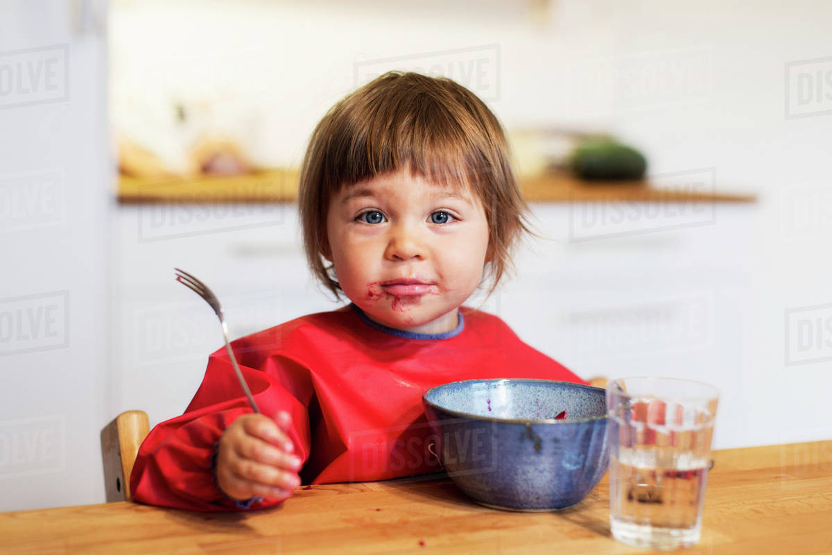 Portrait of little girl with messy mouth eating fruit salad at home ...