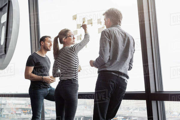 Business colleagues discussing over notes stuck to glass window in ...