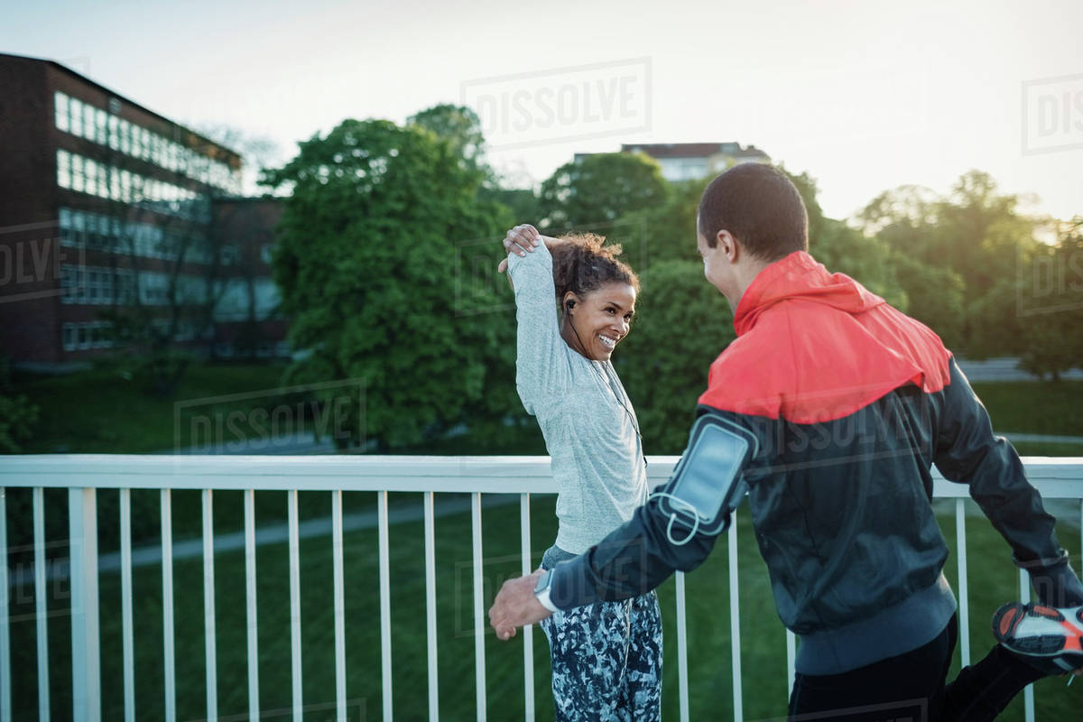 Happy friends stretching while standing by railing - Stock Photo - Dissolve