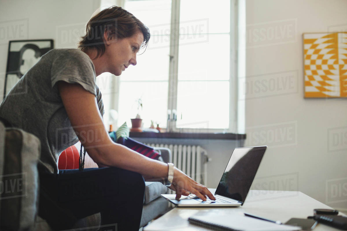 Side view of industrial designer working on laptop in living room ...