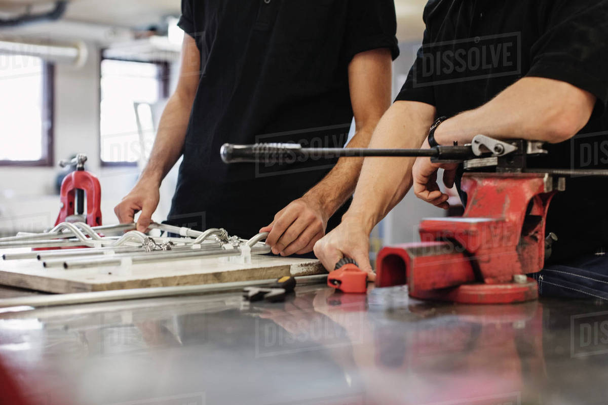 Midsection of auto mechanic teacher and student working at workbench ...