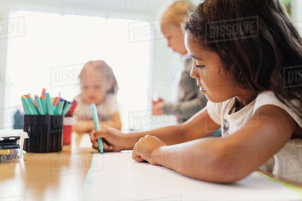 Girl using felt tip pen in drawing class with classmates in background ...