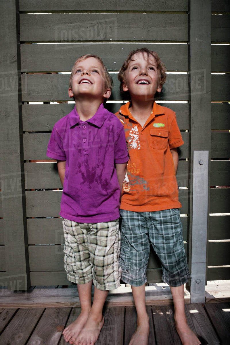 Two playful brothers standing against wooden fence - Stock Photo - Dissolve