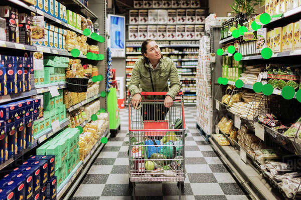 Female customer with shopping cart on alley at supermarket - Royalty ...