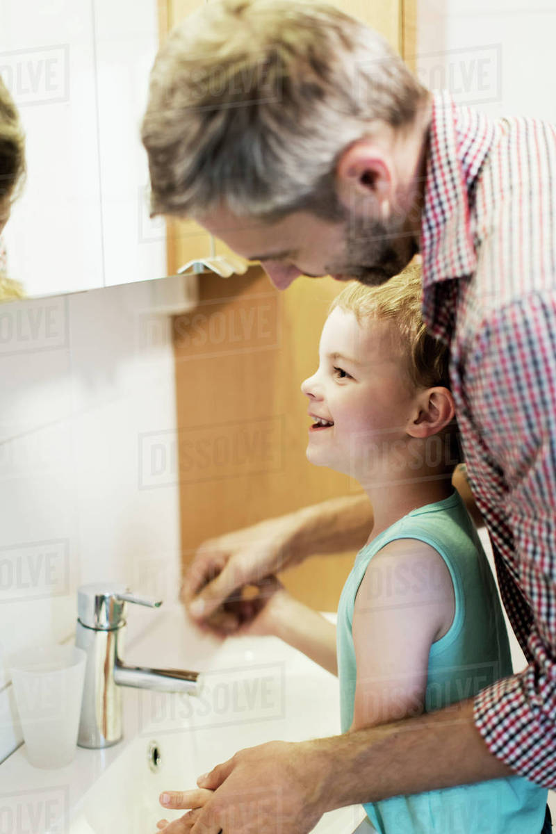 Smiling father washing boy's hands in sink at home - Stock Photo - Dissolve